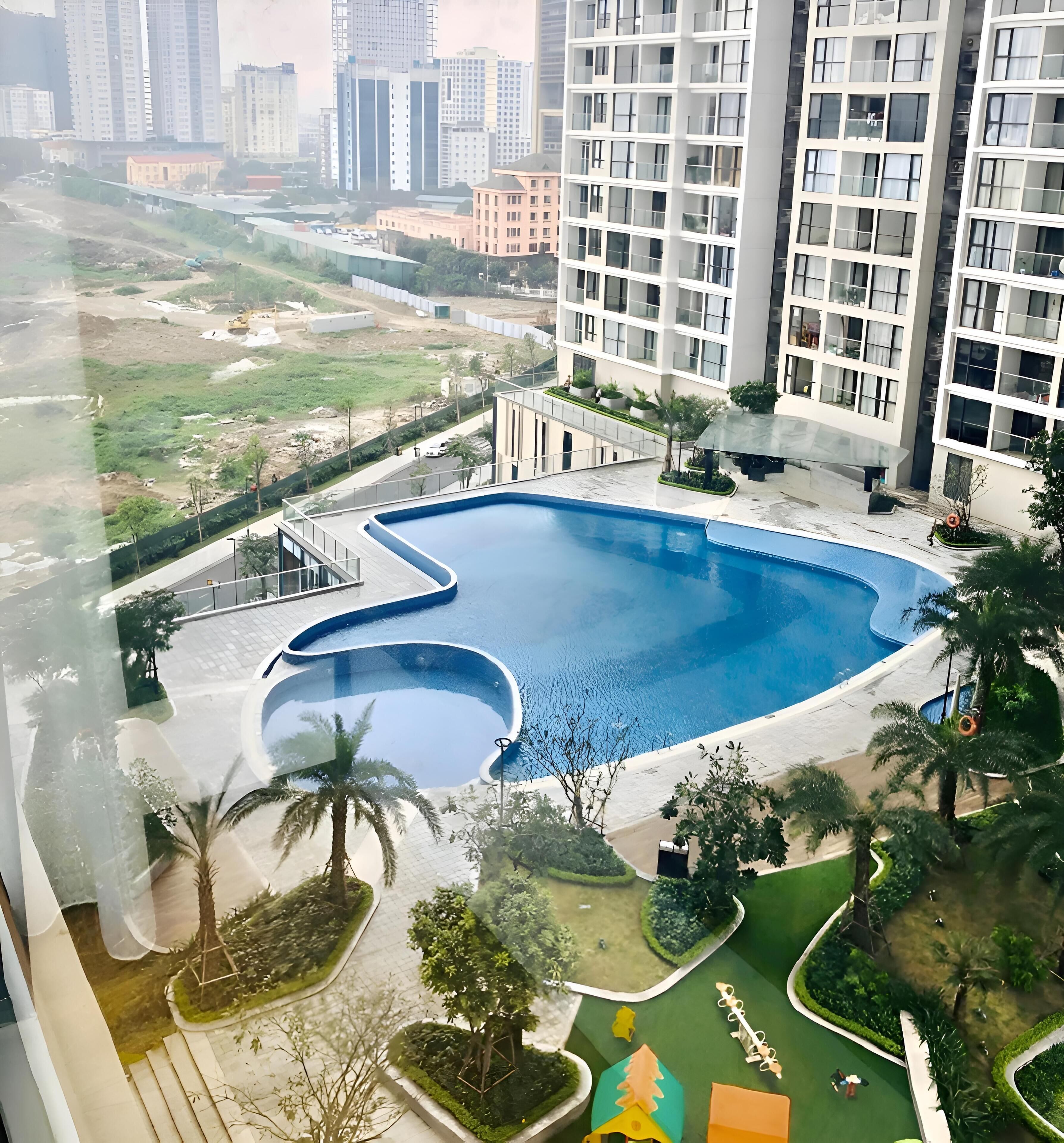 Zona residencial com piscina, rodeada por vegetação e edifícios de apartamentos modernos ao fundo.