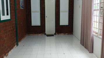 Um corredor com três portas, piso ladrilhado e uma janela com cortinas.