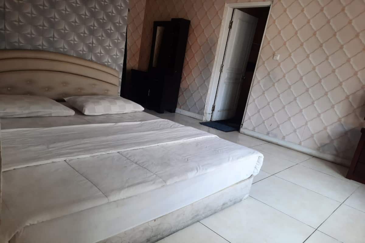 Quarto com uma cama grande, cabeceira, guarda-roupa e porta que dá para outro cômodo.