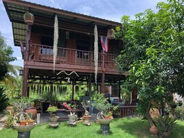 Um edifício de madeira tradicional com varanda, rodeado por vegetação exuberante e plantas em vasos.