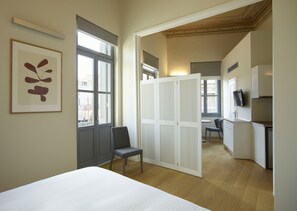 Quarto com cama, cadeira, escrivaninha e cozinha compacta.