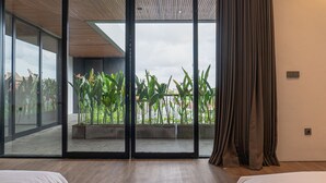 Quarto de hotel moderno com uma grande porta de vidro deslizante que dá para uma varanda externa com plantas.