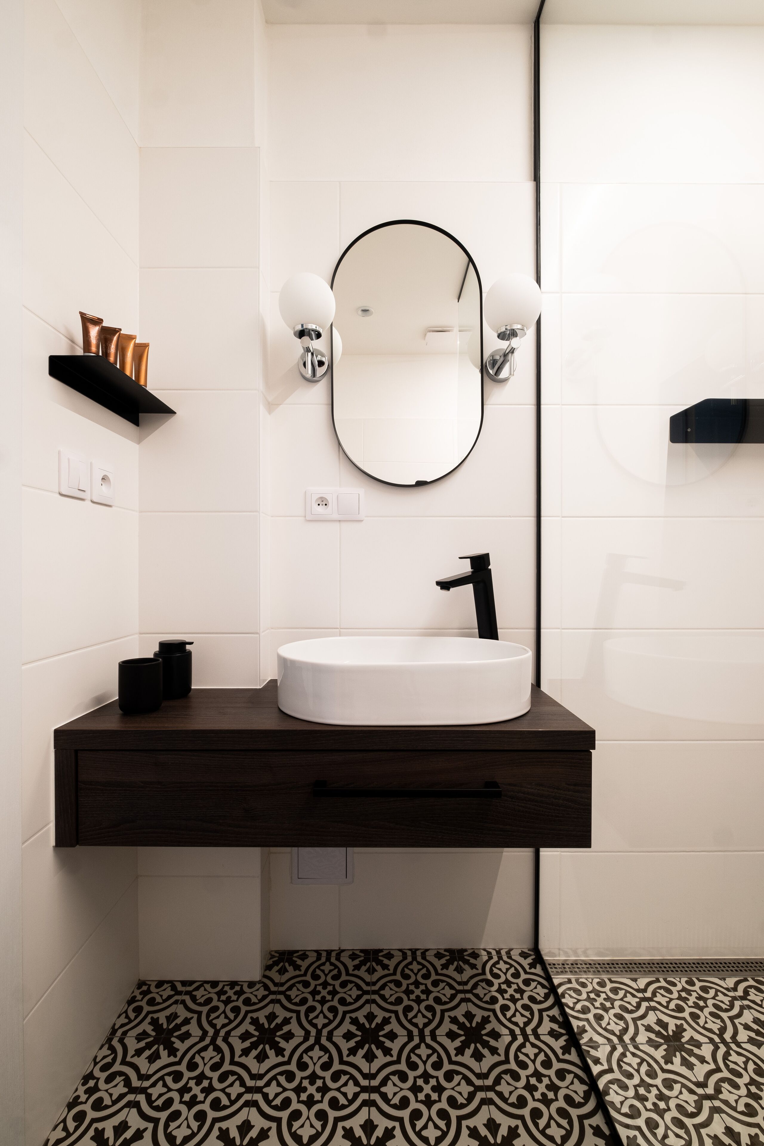 Um banheiro moderno com pia redonda branca, toucador de madeira escura e ladrilhos de piso estampados.