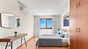 Quarto moderno com escrivaninha de madeira, cama com colcha cinza, espelho grande e janela com cortinas.