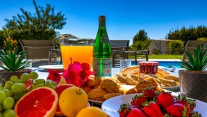 Uma mesa com uma garrafa de água S. Pellegrino, um copo de suco de laranja e diversas frutas e doces.