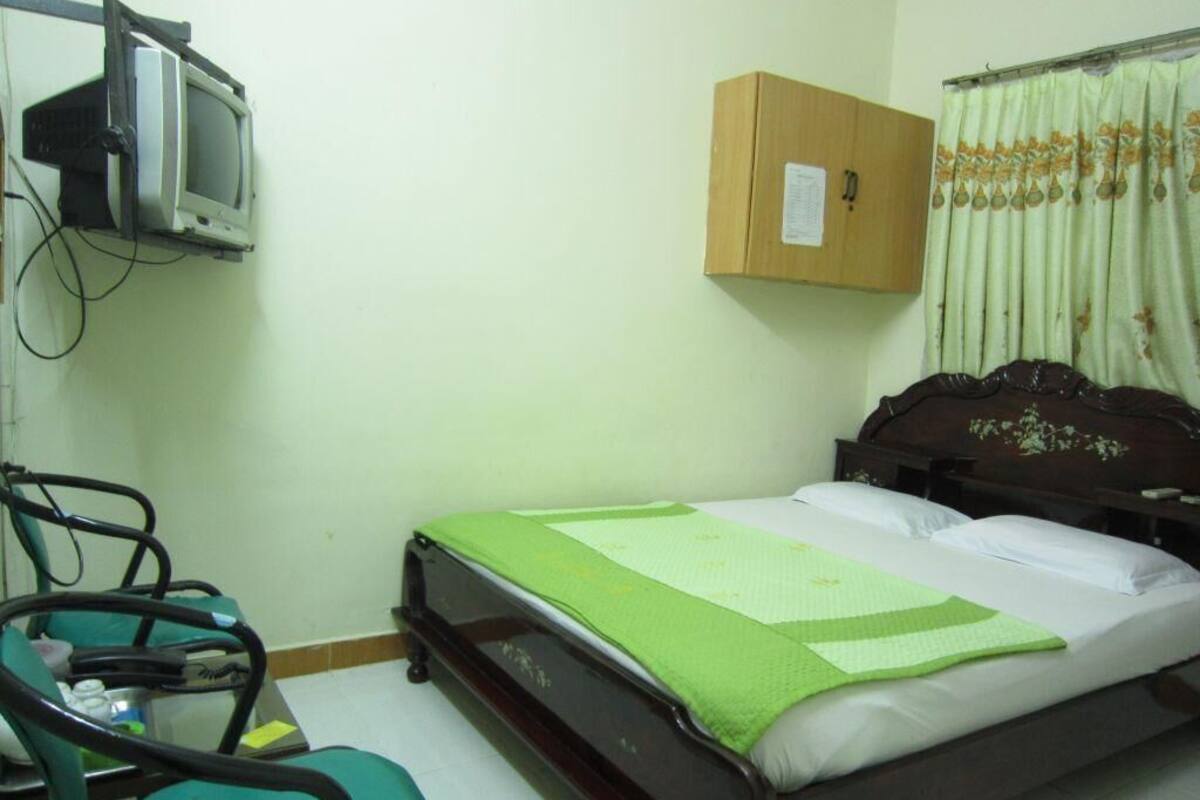 Quarto com cama, um armário de madeira, televisão na parede e uma cadeira.