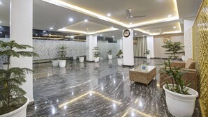 Um hall amplo com piso de mármore polido, diversos vasos de plantas, um balcão de recepção e iluminação de teto moderna.