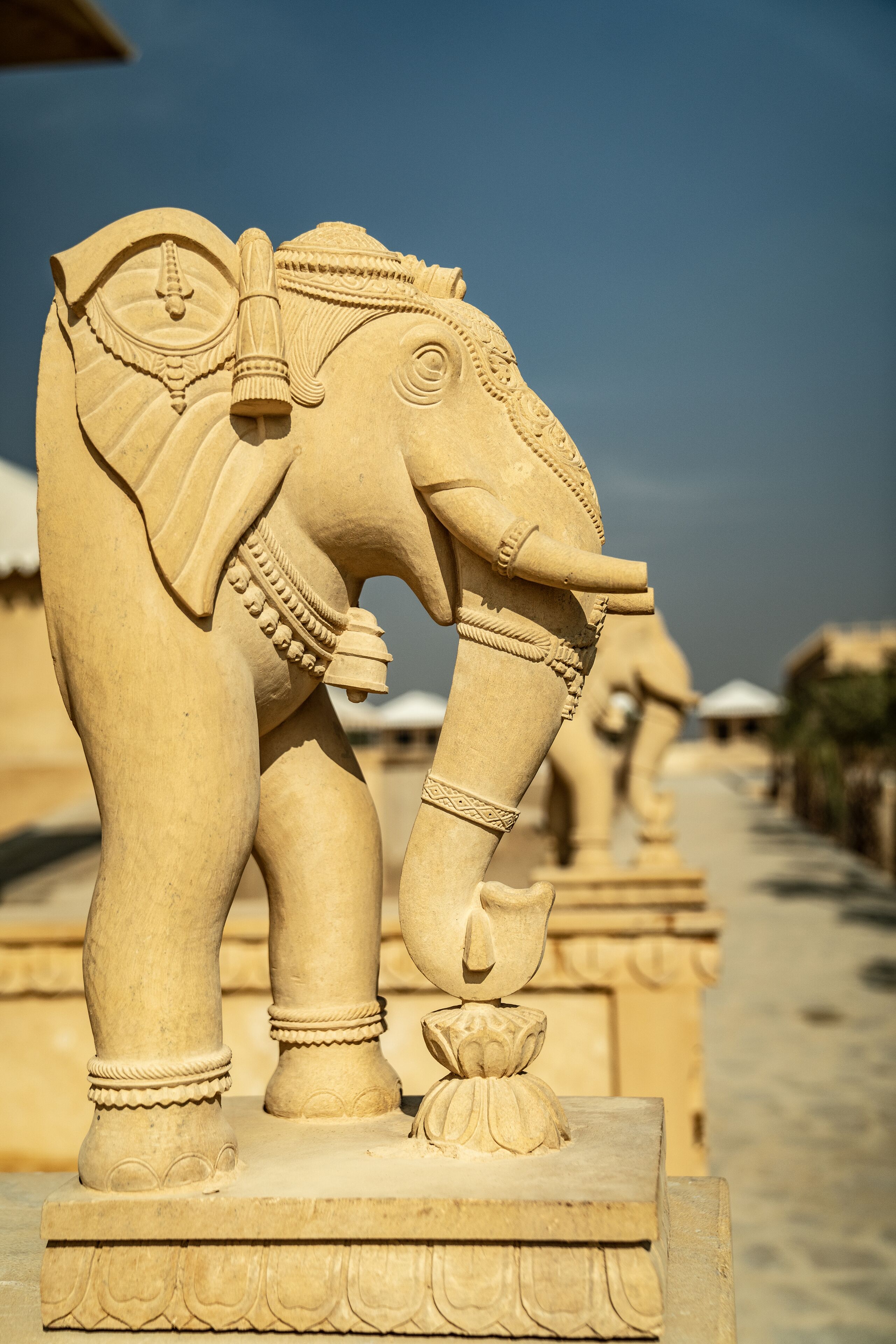 Escultura detalhada de elefante em arenito, com esculturas intrincadas, posicionada sobre um pedestal.
