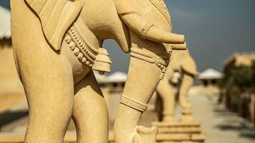 Escultura detalhada de elefante em arenito, com esculturas intrincadas, posicionada sobre um pedestal.