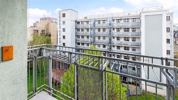Varanda com guarda-corpo de metal dando para um prédio residencial com várias varandas.