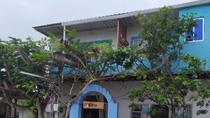 Um edifício com fachada azul, uma parede de pedra e uma árvore em frente.