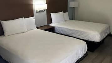 Quarto de hotel com duas camas de solteiro, mesa de cabeceira com abajur e luminária na parede.
