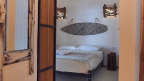 Quarto com cama, prancha de surf decorativa na parede e duas luminárias.