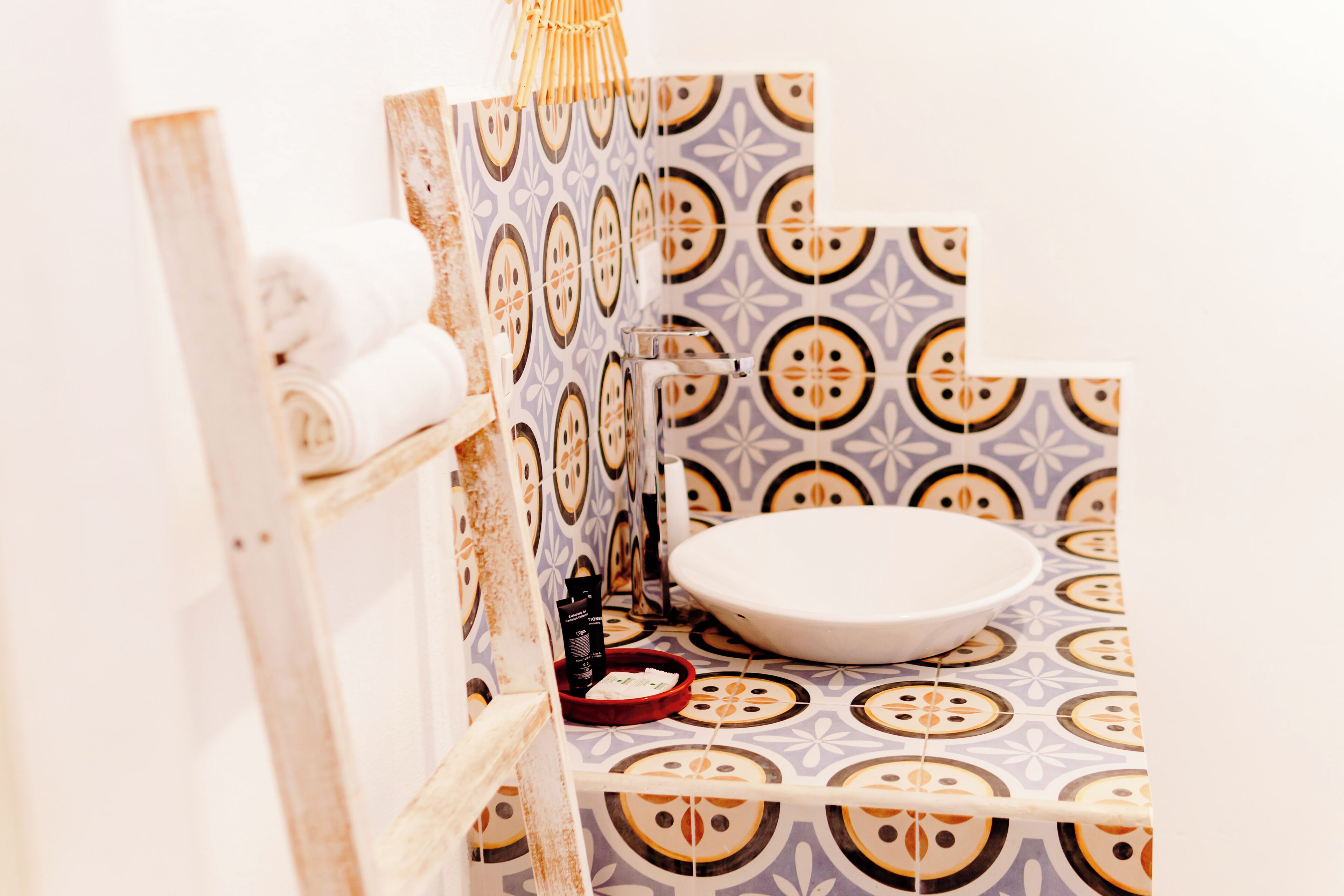 Casa de banho com azulejos estampados, uma cadeira de madeira e uma pia branca.