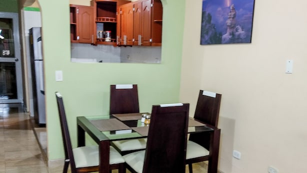 Uma área de refeições com mesa e cadeiras, cozinha ao fundo e um quadro na parede.