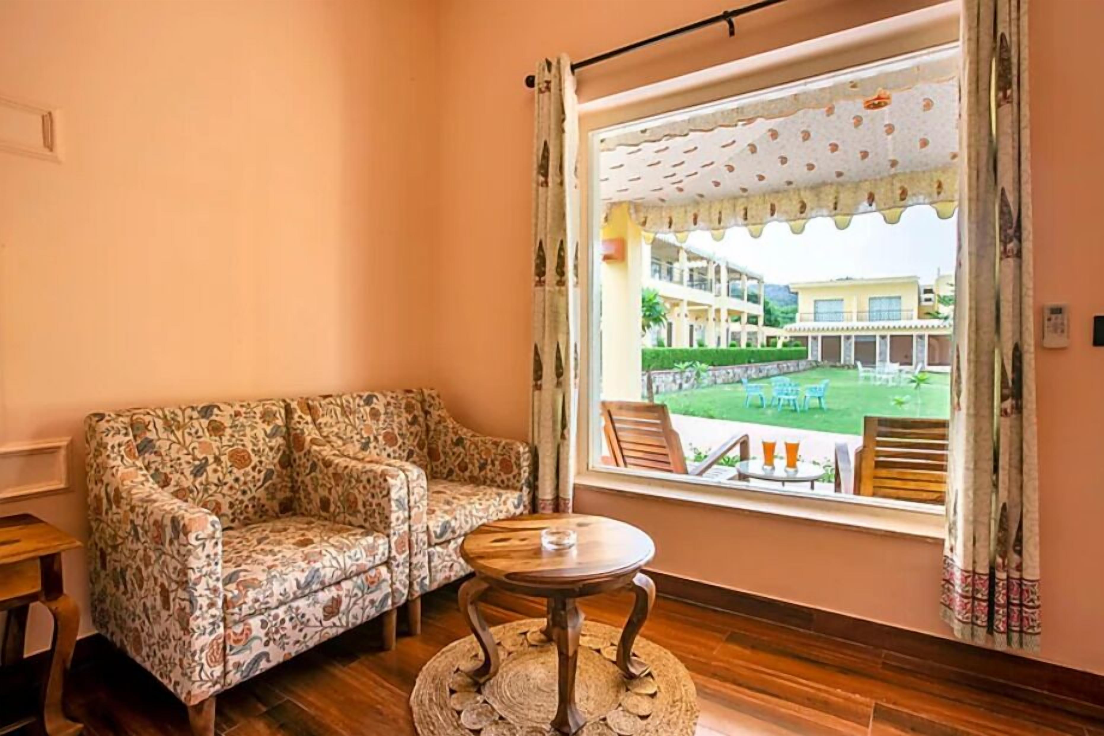 Quarto com sofá estampado, uma pequena mesa redonda e vista para um pátio com mobiliário de exterior.