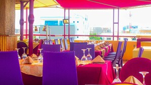 Restaurante com mesas ao ar livre, preparadas para servir com copos de vinho e guardanapos, e vista para edifícios ao fundo.