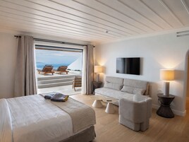 Quarto de hotel com cama, sofá, televisão e vista para o mar.