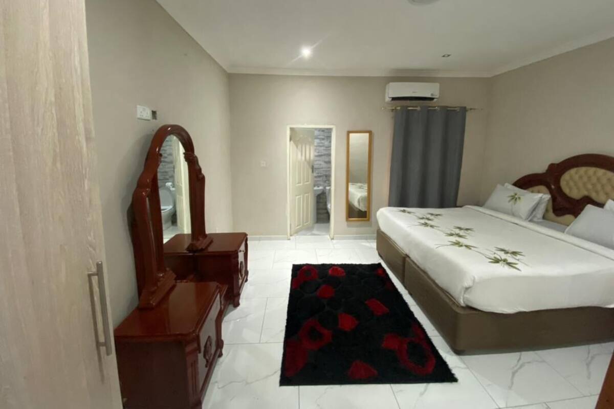 Quarto com cama, cômoda, espelho e porta para um banheiro.