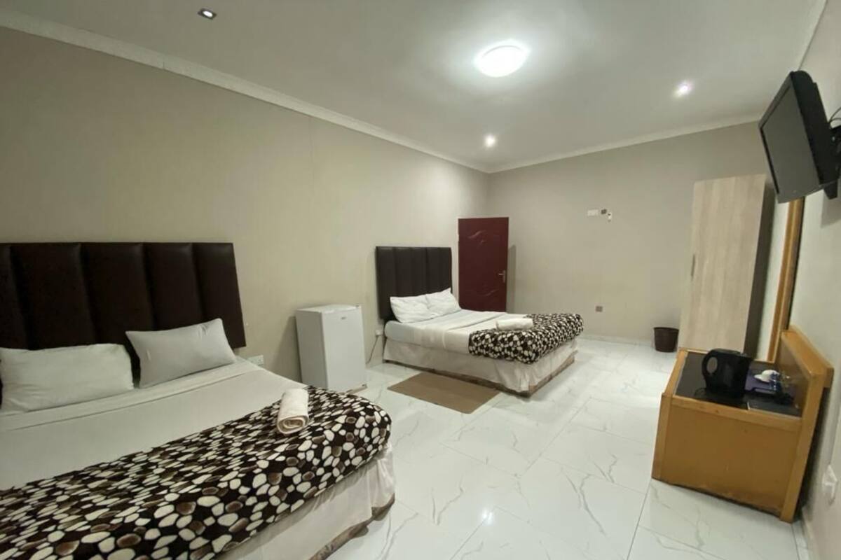 Quarto de hotel com duas camas, uma televisão e uma mesa de cabeceira de madeira.