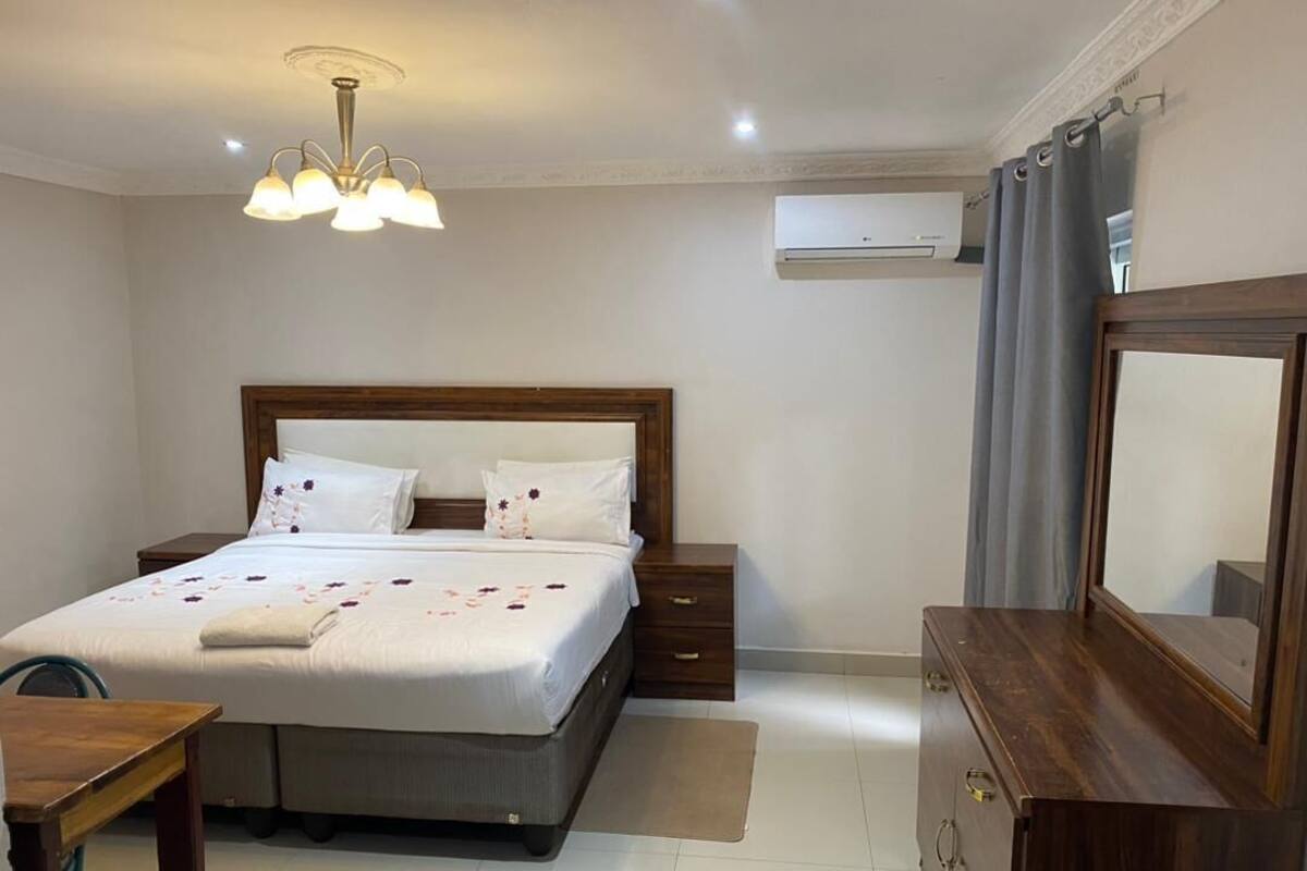 Quarto com cama, mesas de cabeceira, cômoda, espelho, ar-condicionado e luminária de teto.