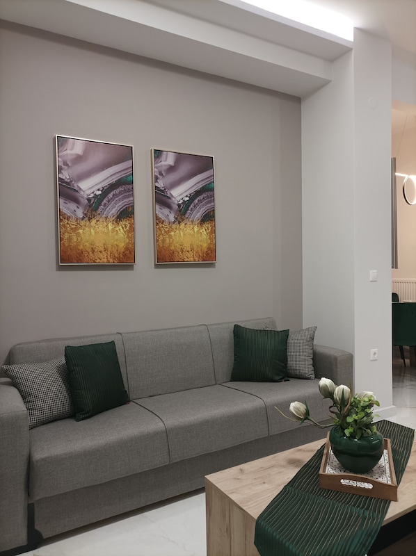 Uma sala de estar moderna com um sofá cinza, duas pinturas abstratas e uma mesa de centro de madeira com uma planta verde.