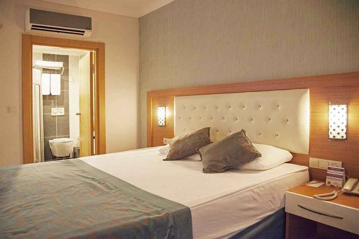 Quarto de hotel com cama, mesa de cabeceira e banheiro visível por uma porta aberta.