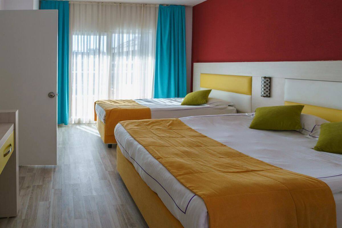 Quarto de hotel com duas camas, um guarda-roupa e uma janela com cortinas.