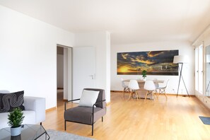 Uma sala de estar moderna com área de jantar, sofá, mesa de centro e uma pintura de um pôr do sol na parede.