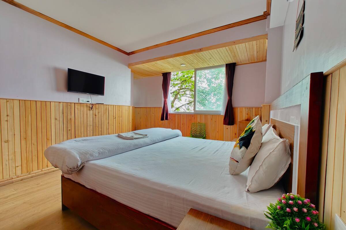 Uma cama de casal com cabeceira de madeira, uma TV de tela plana na parede e uma janela com cortinas.