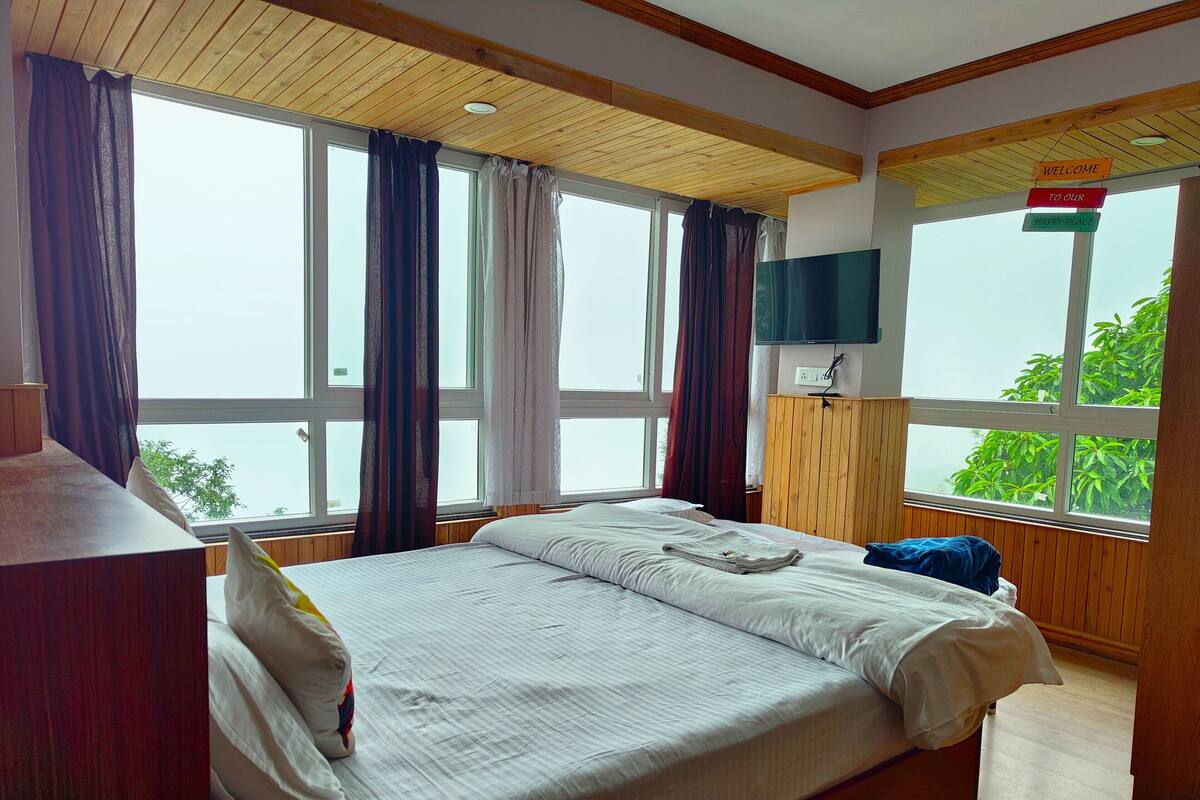 Quarto de hotel com cama grande, teto de madeira e TV fixada na parede.