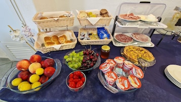 Mesa de buffet com diversos alimentos, incluindo frutas, doces, carnes e acompanhamentos.