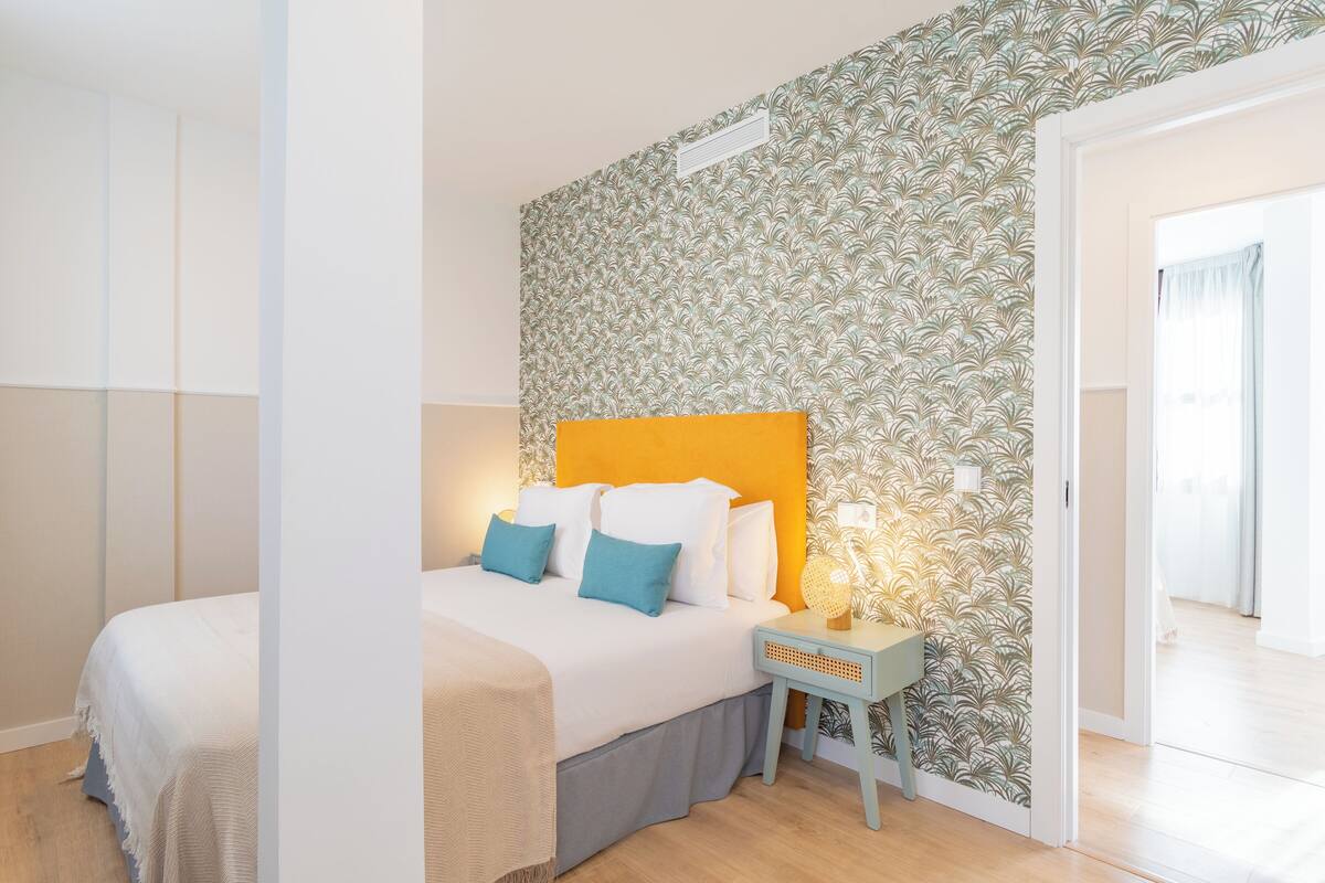 Quarto com cama, mesa de cabeceira e papel de parede estampado.