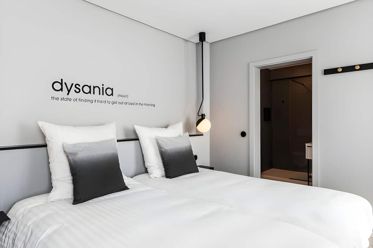 Um quarto moderno com uma cama grande, roupa de cama branca e luminária fixada na parede.