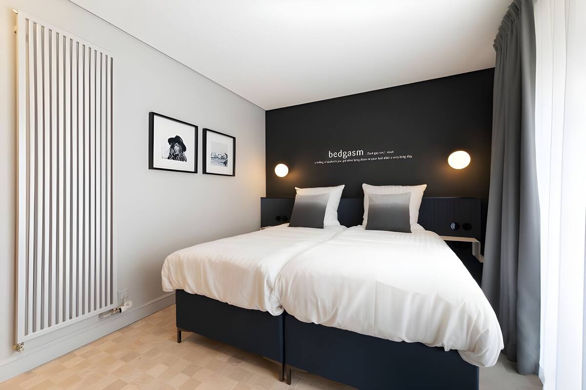 Quarto moderno com cama, mesas de cabeceira, luminária na parede e radiador.