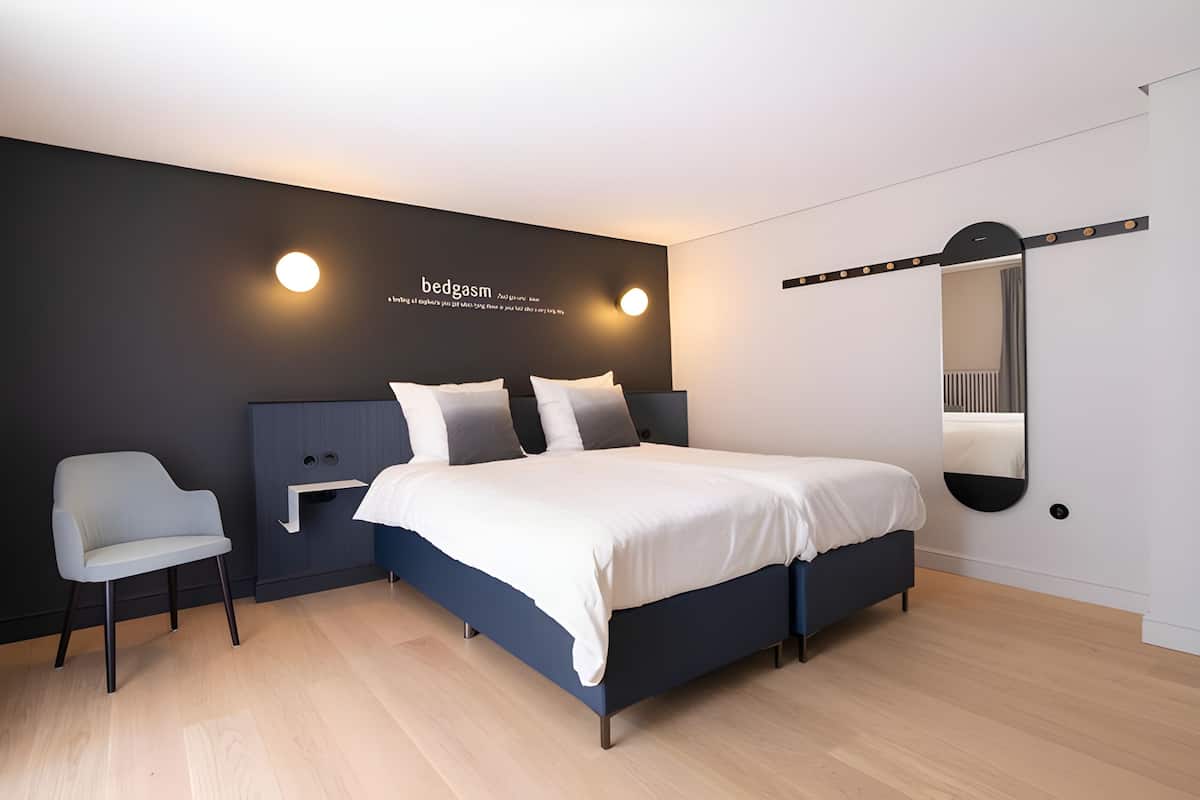 Um quarto moderno com cama, mesas de cabeceira, uma cadeira, um espelho e uma luminária na parede.
