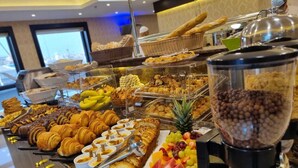 Buffet com diversos pastéis, frutas e uma máquina de café.