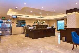Uma área de recepção de hotel com piso de mármore, um balcão de atendimento, uma cadeira azul e uma grande janela com vista para a cidade.