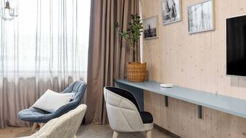 Quarto com teto de madeira, uma janela grande com cortinas, televisão fixada na parede e duas cadeiras.