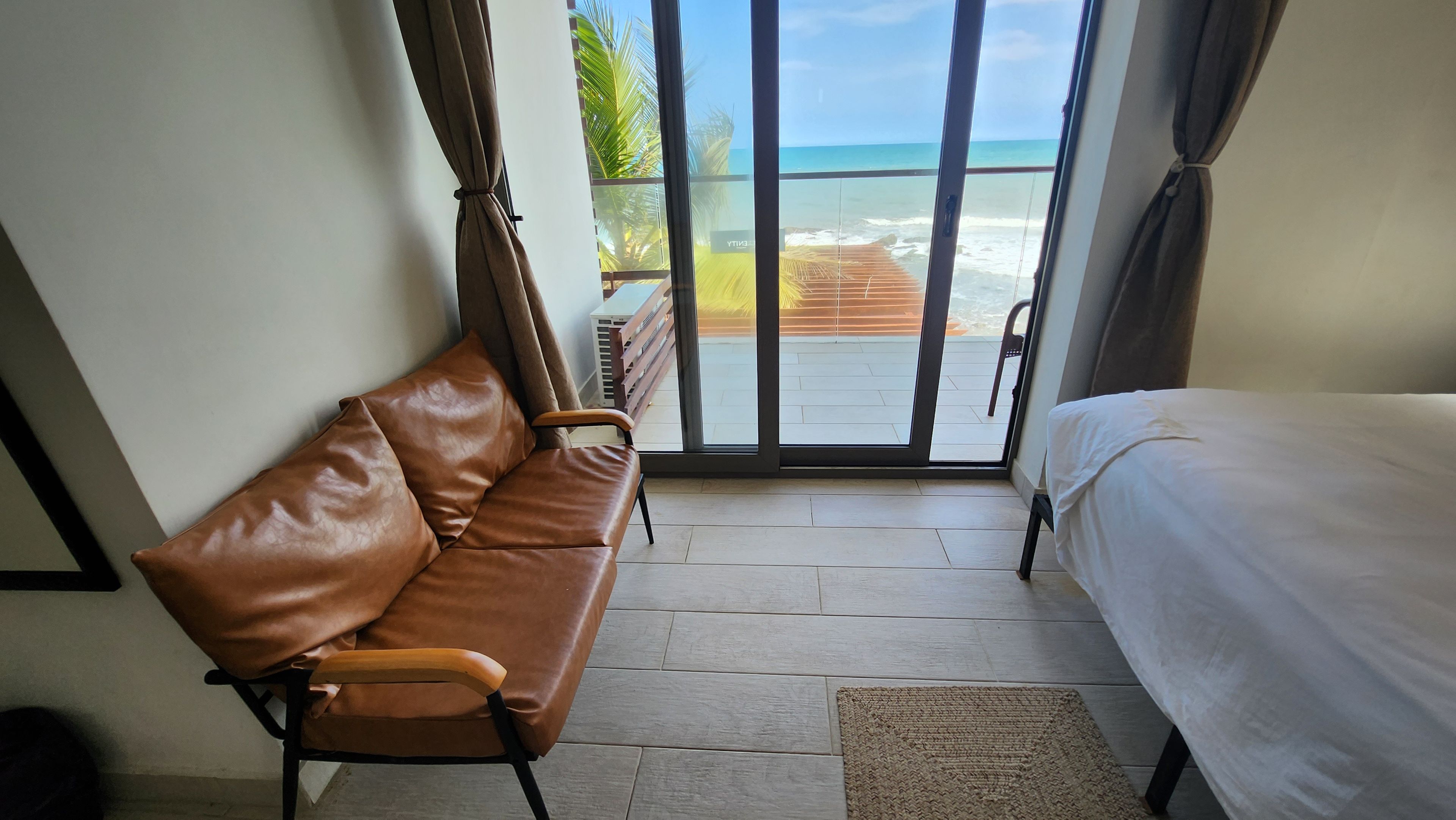 Quarto com cama, sofá de couro, vista para o oceano e porta de correr de vidro.