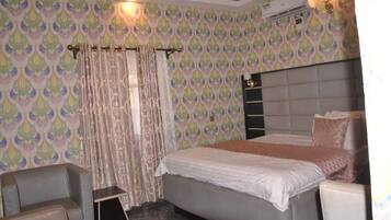 Quarto de hotel com uma cama, uma cadeira, uma mesinha e papel de parede estampado.