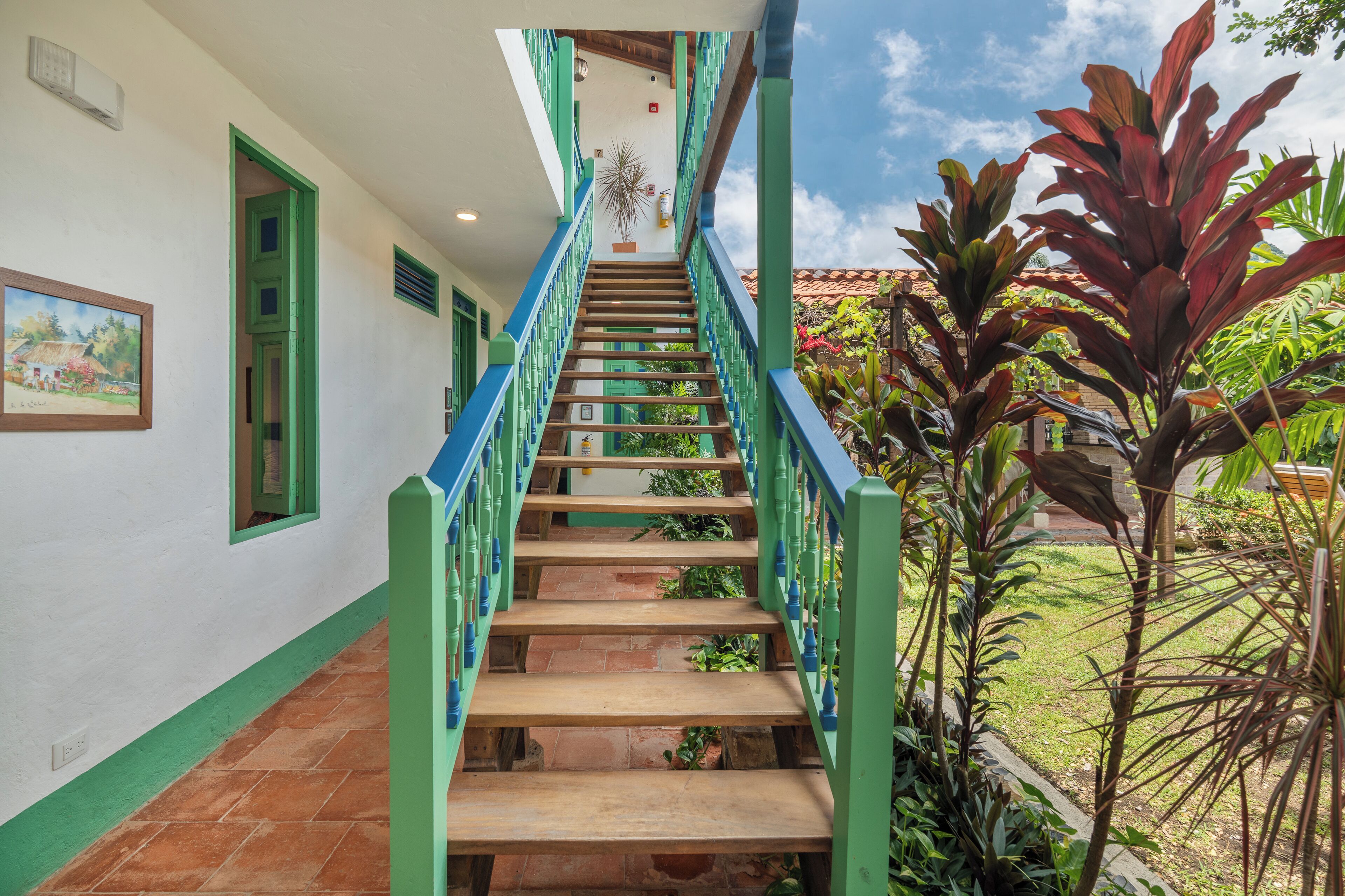 Uma escadaria com corrimãos verdes leva a um patamar com uma planta e um aplique de parede.