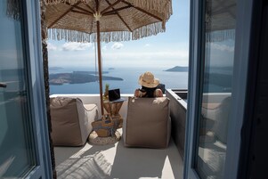 Varanda com vista para o mar, com uma cadeira, uma mesa pequena e um guarda-sol de tecido.