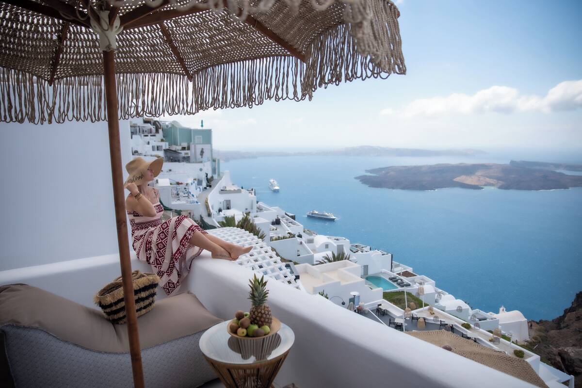 Uma varanda com vista para o mar, edifícios brancos e uma mesa com frutas.