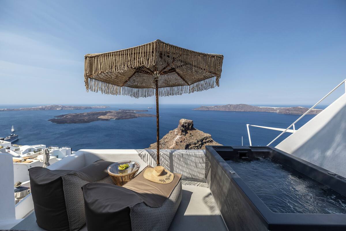 Uma varanda com um guarda-sol de palha, uma banheira de hidromassagem e vista para o mar e ilhas.