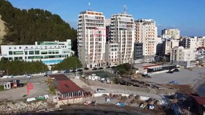 Um edifício com várias andares, varandas, área de estacionamento e uma construção nas proximidades.