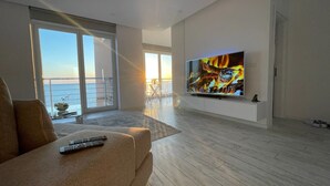 Sala de estar moderna com uma televisão de tela plana grande, um sofá e vista para o mar através de grandes janelas.