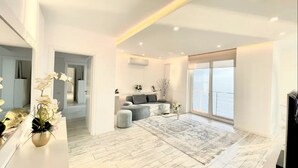 Uma sala de estar moderna com um sofá cinzento, uma mesa de centro e uma janela grande com vista para o mar.
