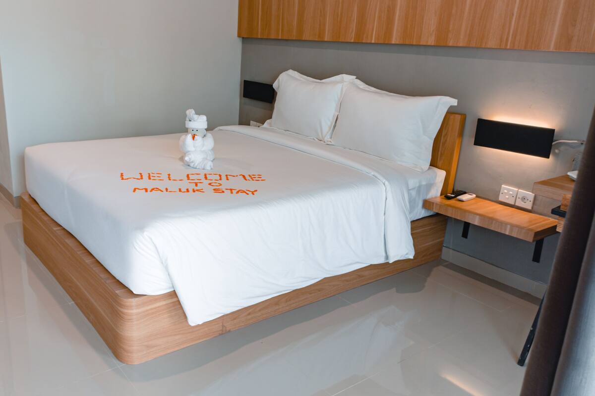 Quarto de hotel moderno com uma cama bem arrumada, uma mesa de cabeceira com abajur e televisão na parede.