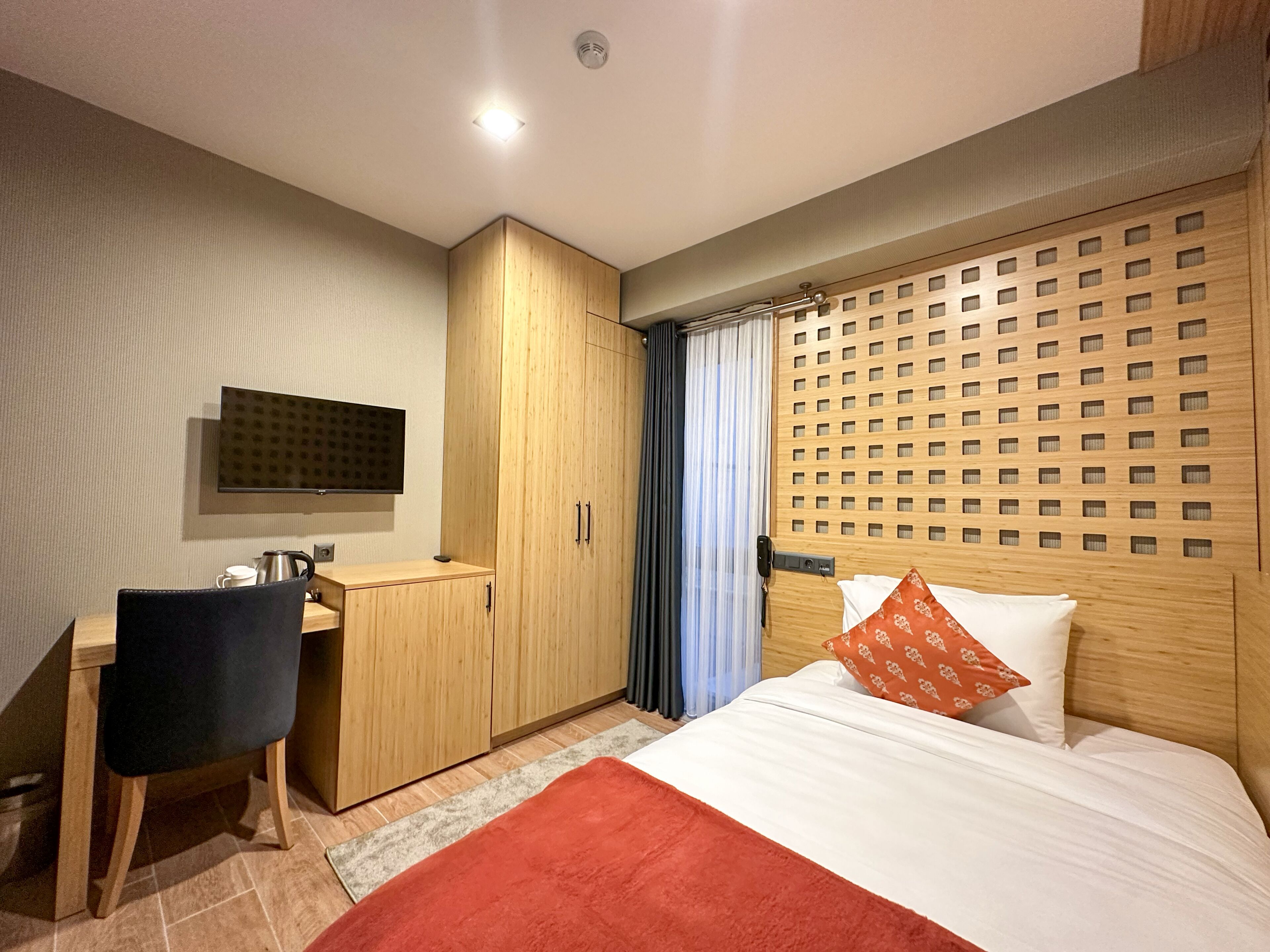 Quarto de hotel com cama, escrivaninha, armário e televisão presa na parede.